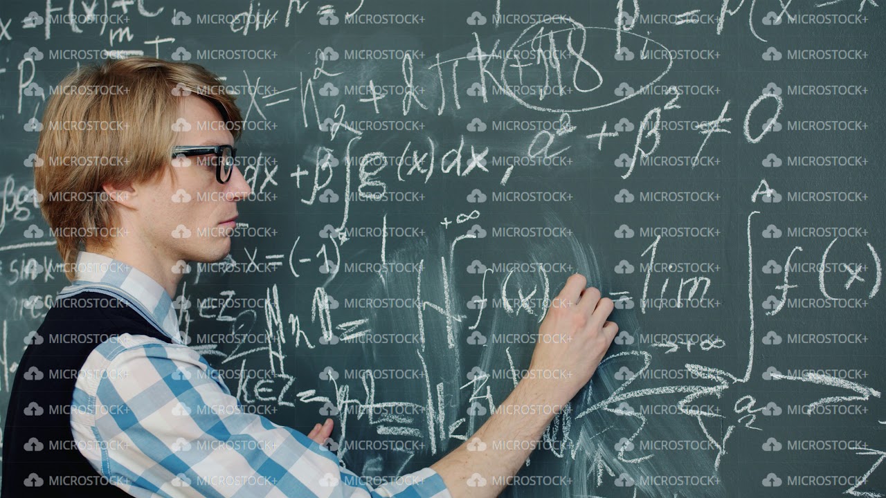 Smart man writing equations on blackboard in class focused on ...