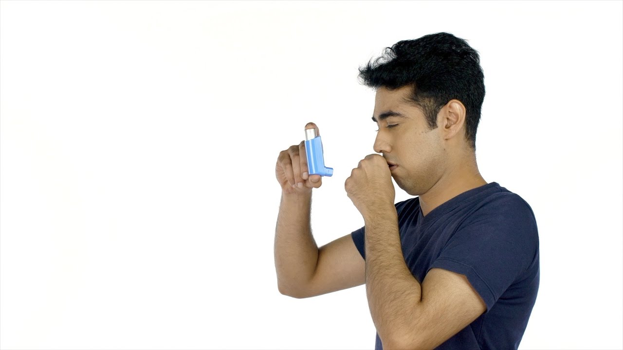 Young asthma patient using a medical spray against the white b ...