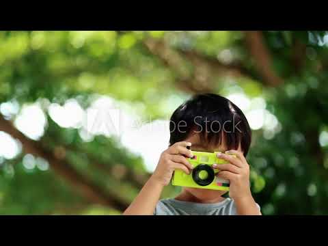 Asian child takes photo with toy camera on nature green bokeh background