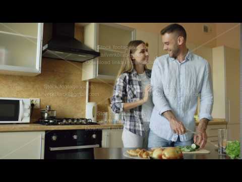 Happy young couple kissing embracing and chatting in the kitchen while cooking breakfast at home