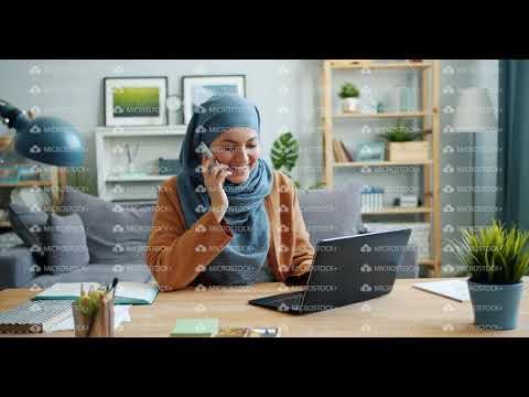 Slow motion of girl in hijab using laptop then talking on mobile phone at home