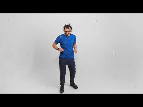 Cheerful young adult guy is walking straight looking at camera and listening to music in earphones
