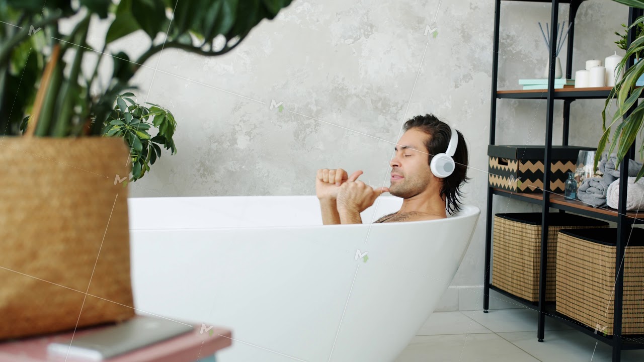 Joyful guy dancing enjoying music through headphones taking bath in ...