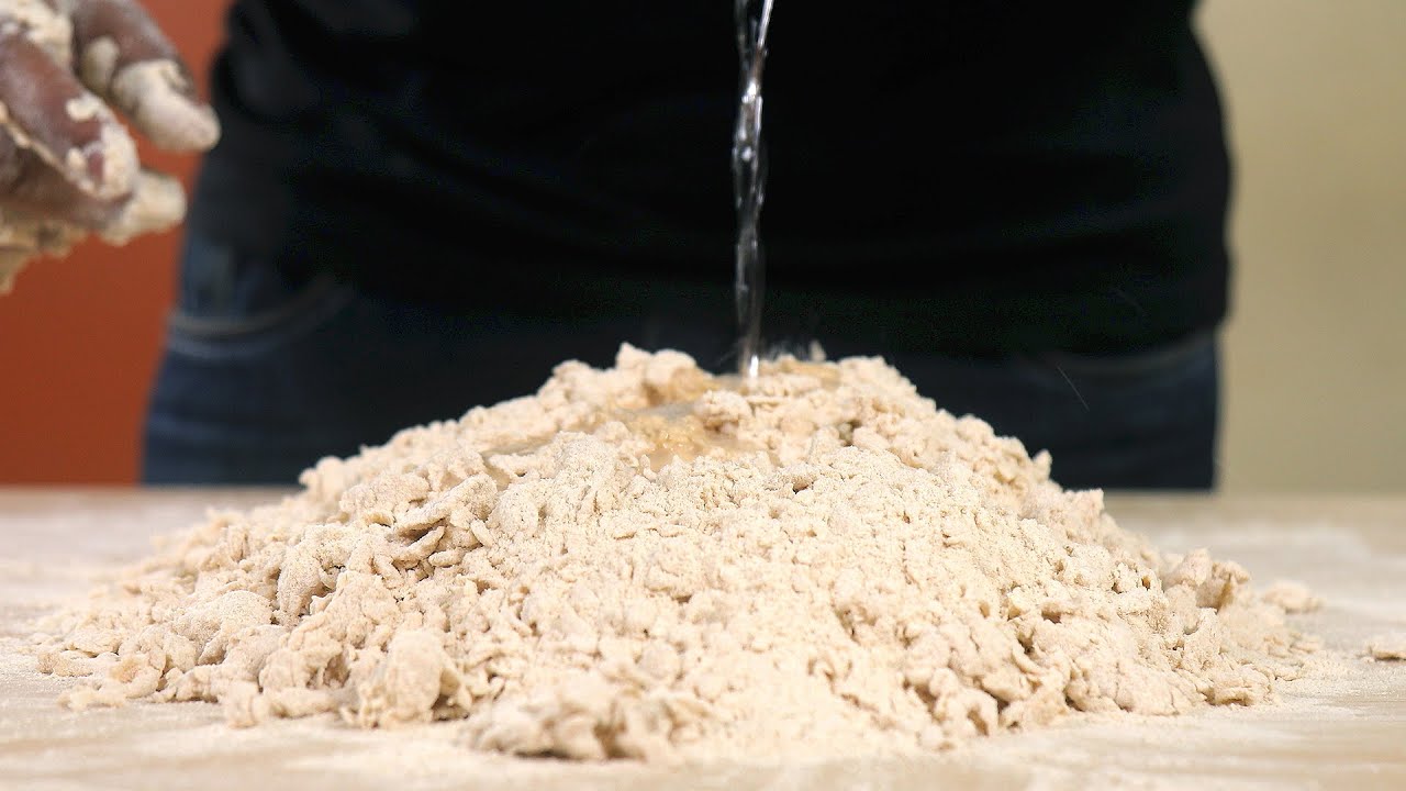 Close up shot of a man mixing water in wheat flour while knead ...