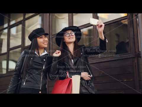 Excited female friends beautiful girls are taking selfie with smartphone and holding paper bags with