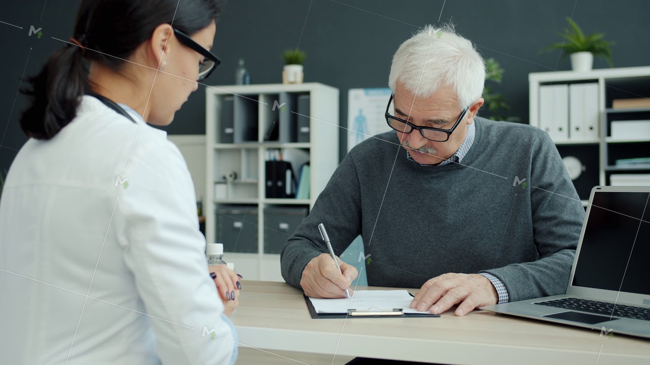 Elderly man patient signing medical papers during consultation with ...
