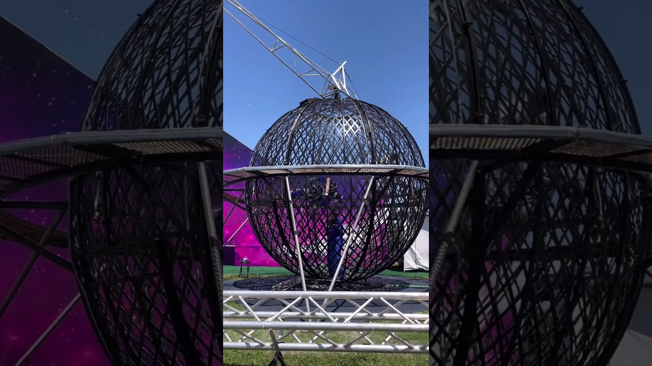 Man Riding Motorcycle Inside Steel Cage with his Wife Standing in the ...