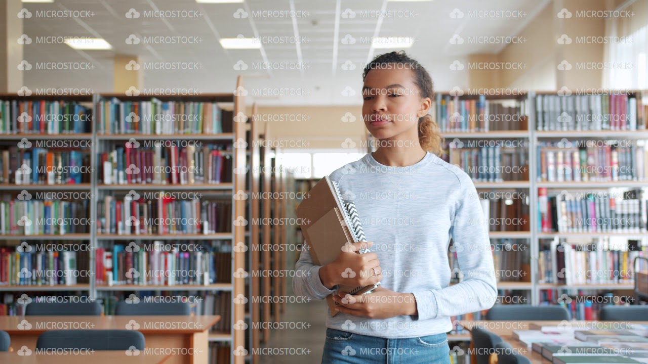 African American girl walking in university library holding books ...