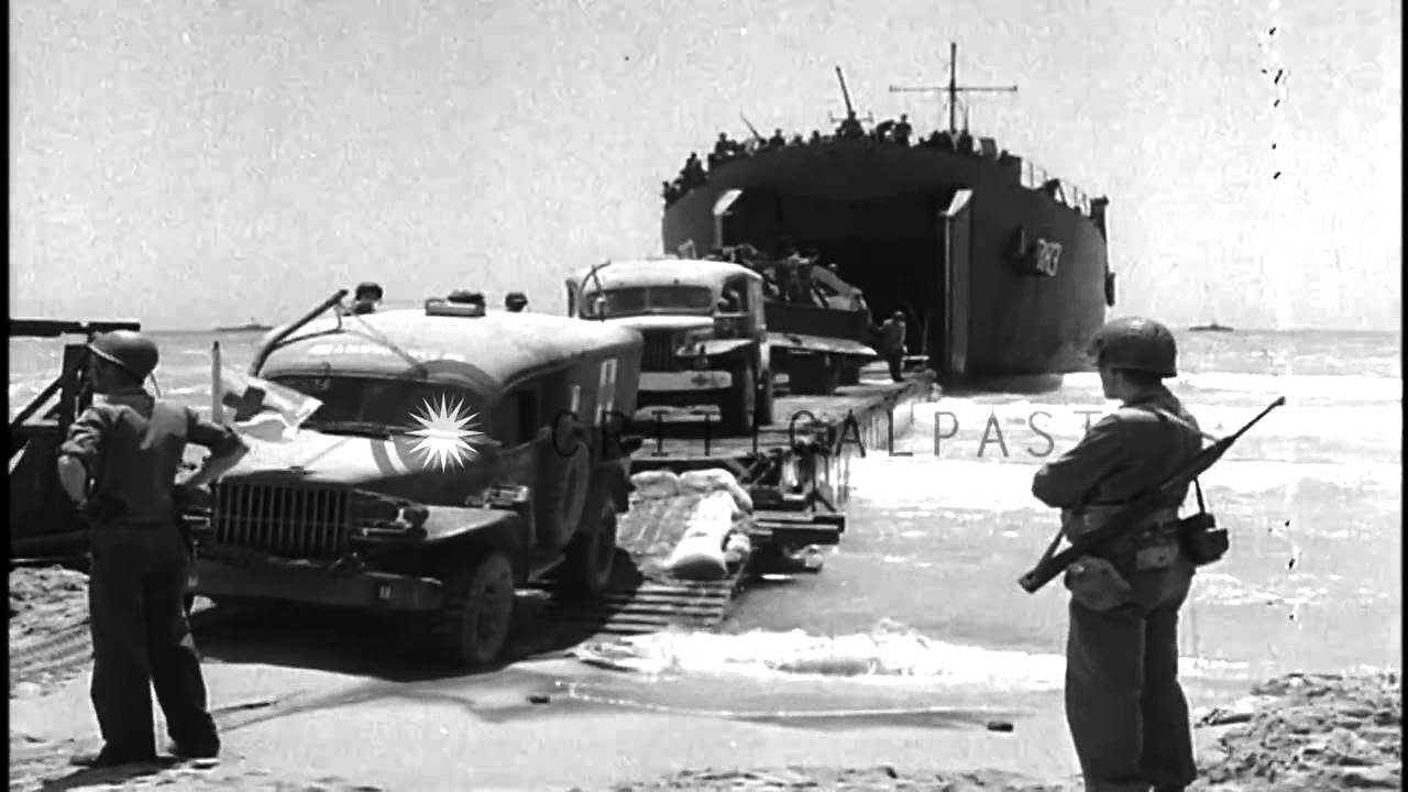 Trucks and other vehicles drive from LST onto pontoon causeway to shore ...