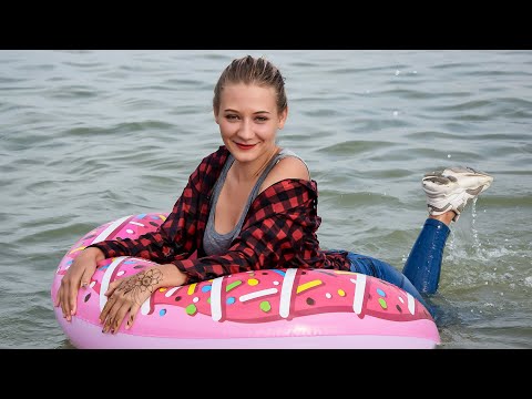A GIRL IN CLASSIC WET CLOTHES ON AN INFLATABLE CIRCLE POSE COOLLY ON THE SEA SHORE FOR WETLOOK VIDEO