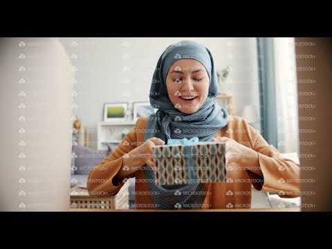 Slow motion of happy mixed race lady in hijab opening box taking present smiling