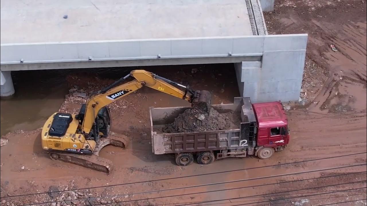 Excavator Digging The Mud Under A Bridge To Refill The Bucket Of A Dump ...