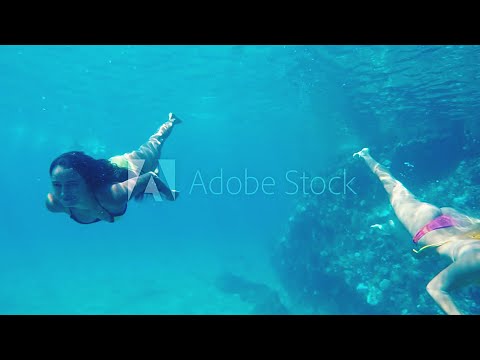Beautiful girls in bikinis swimming underwater holding hands in pacific ocean.