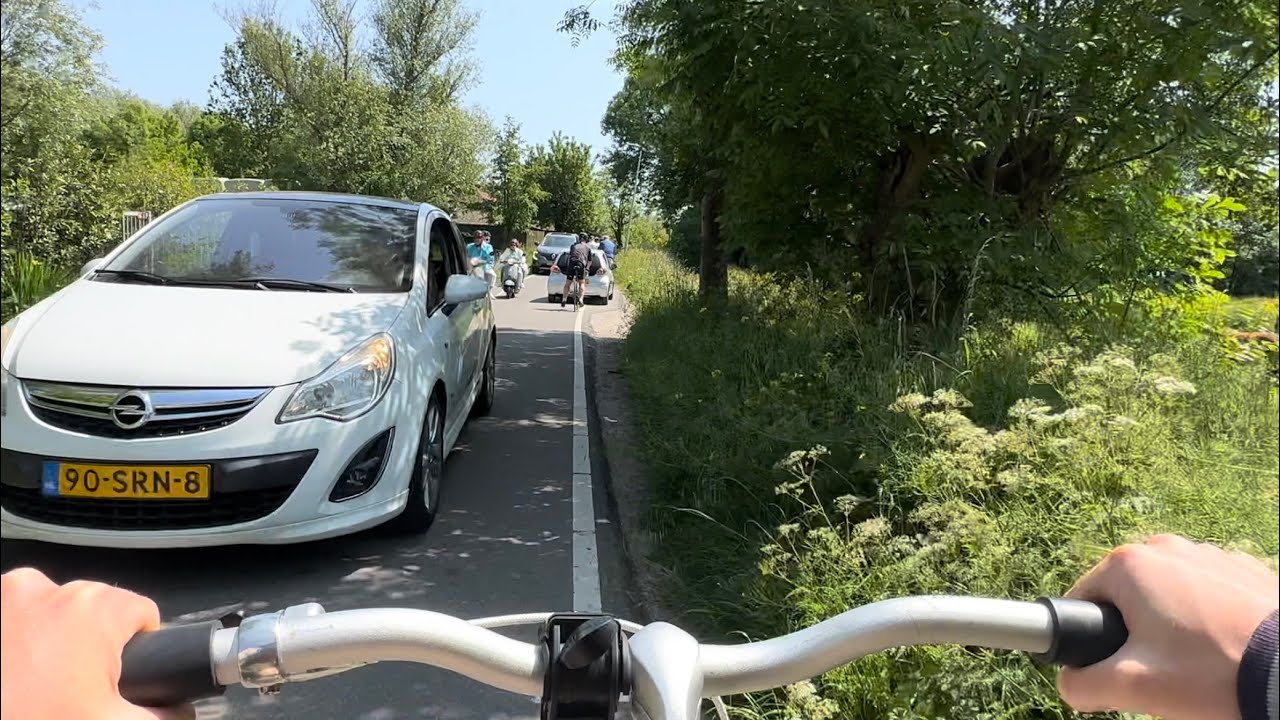 narrow one-lane road congested by cars and cyclists on sunny Saturday ...