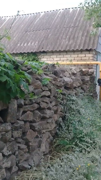 Старинная казачья каменная изгородь с вьющимся хмелем возле дома в