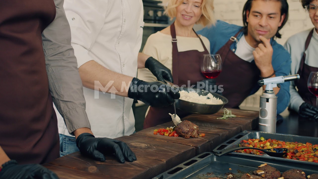 Skilled cook teaching group of students to cook meals with fire, people ...