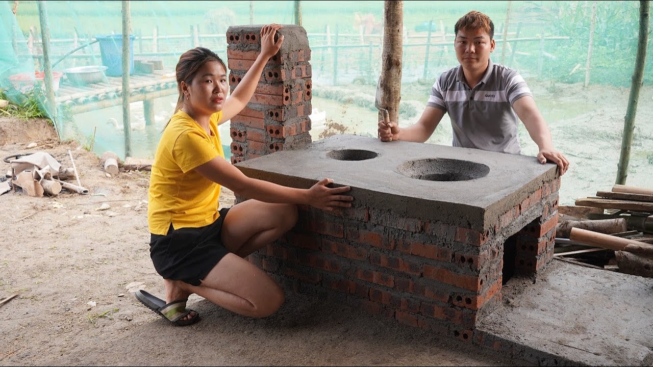 A rural boy and girl build a wood stove with red bricks and cement to ...