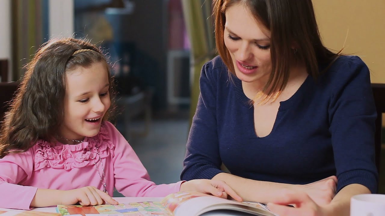 Close-up mother teaching little daughter, reading color book. Stock ...