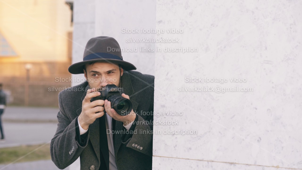 Young male spy agent wearing hat and coat photographing criminal people ...