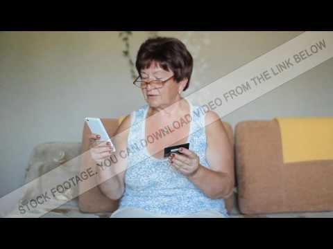Happy mature woman using credit card and phone at home