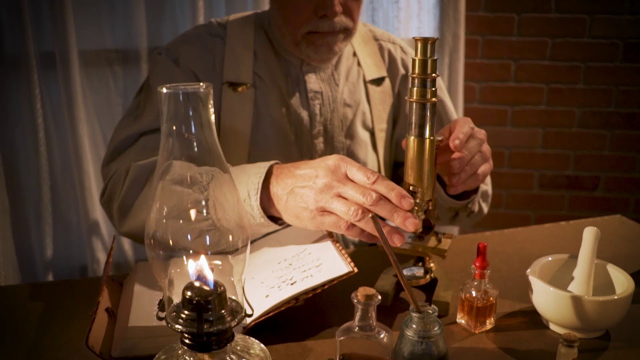 camera moves over desk to 1885 scientist using microscope - YouTube