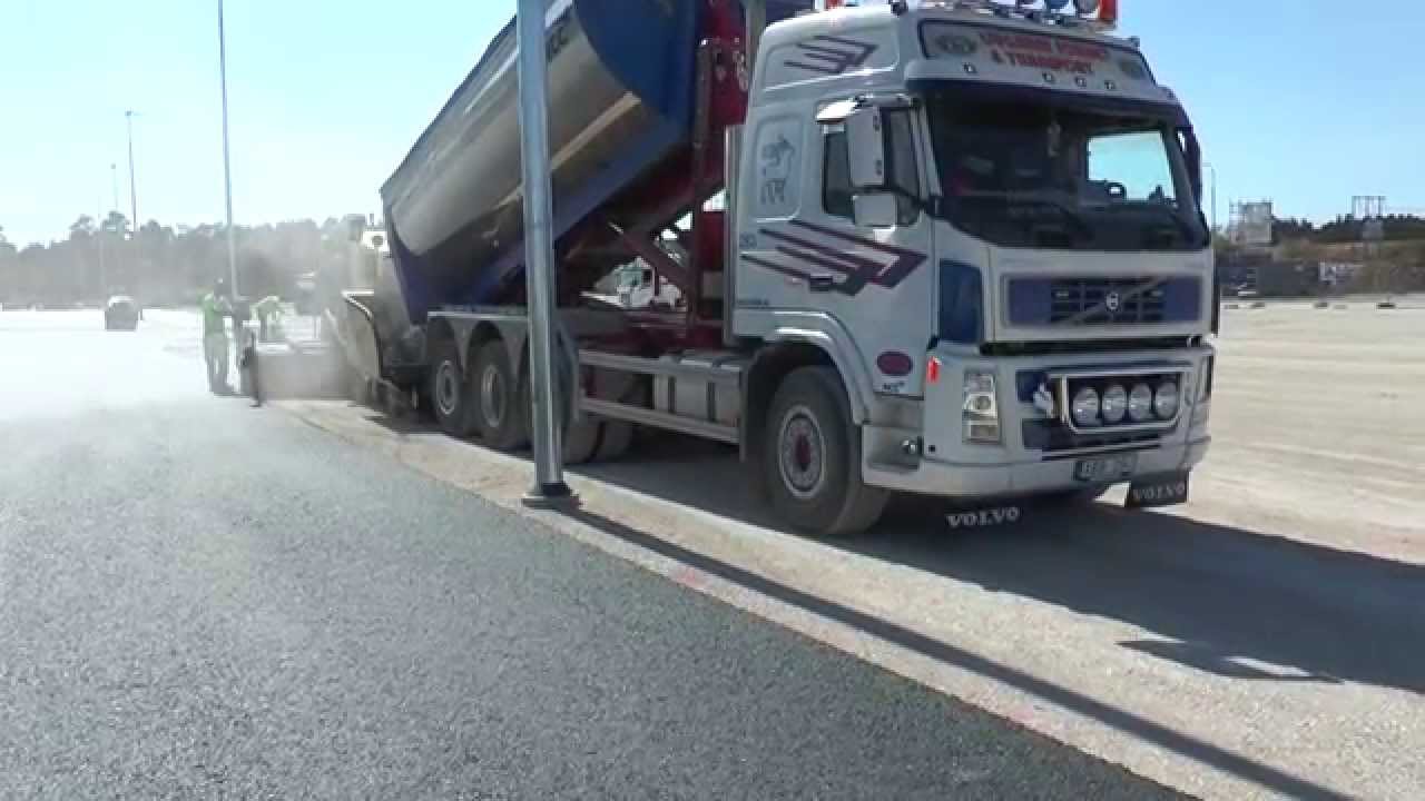Volvo and Scania trucks lay asphalt on a large parking lot outside the ...