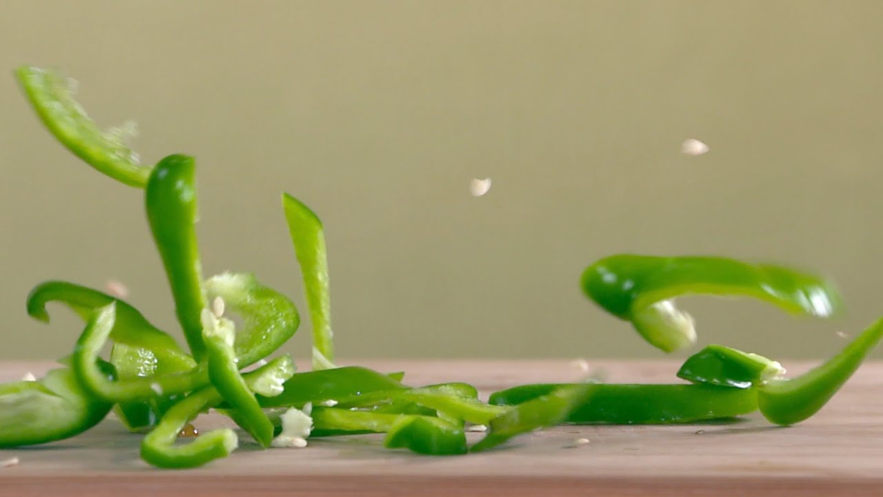 Chopped green capsicum falling on the chopping board in slow m ...