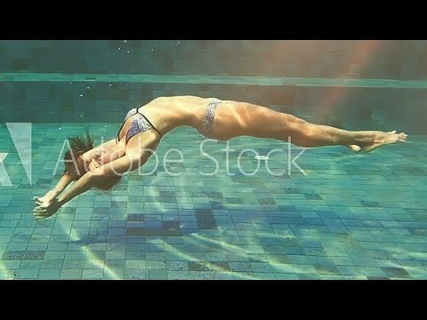 Girl in bikini swimming underwater in blue pool. Cinematic slow motion video.