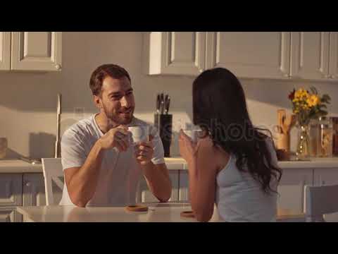 Brunette woman looking at man, giving cup and man drinking coffee, smiling and talking in kitchen