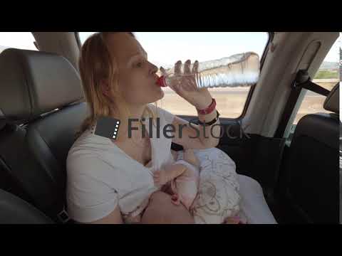 Mum nursing baby and drinking water in moving car