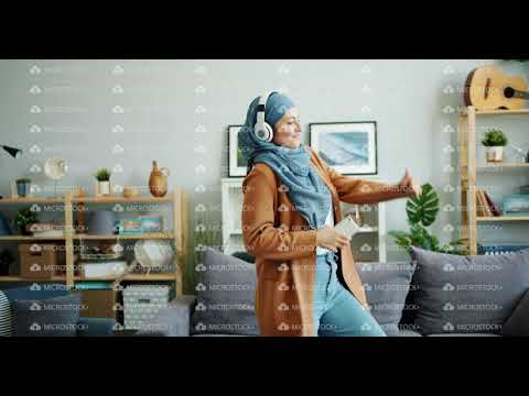 Slow motion of happy mixed race girl in hijab dancing in headphones at home