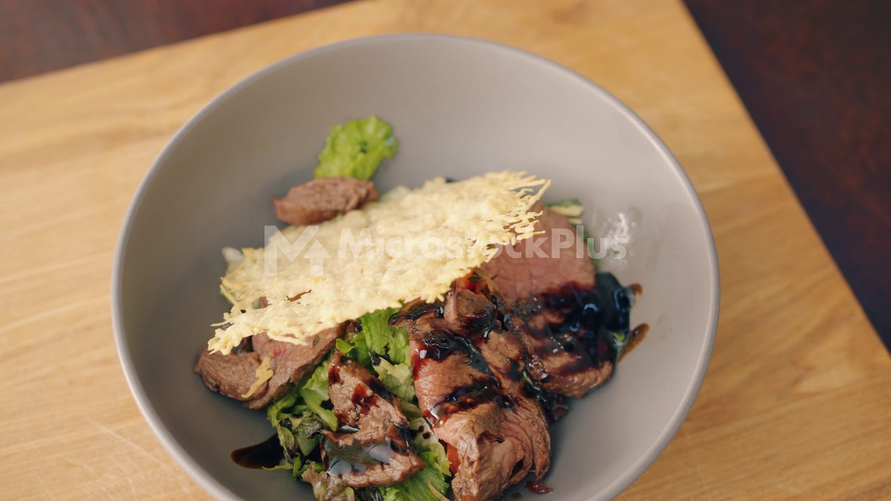 Close-up of bowl of cooked food meat and vegetables on wooden table in ...