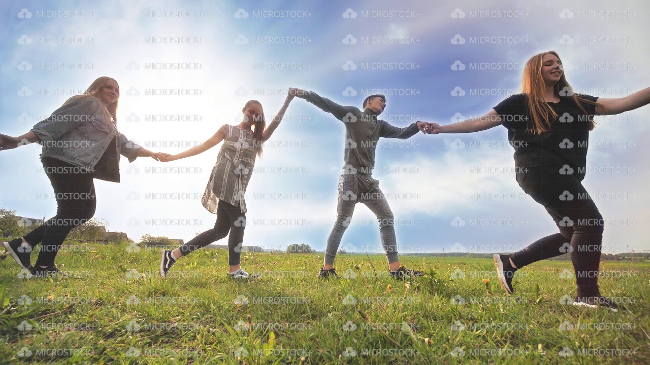 A group of young people lead a round dance holding hands on a summer ...