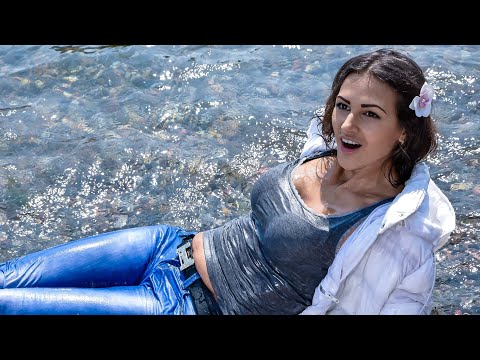 A SLIM MODEL IN A WARM WET JACKET AND JEANS POSE BRIGHTLY ON THE BEACH BY THE SEA FOR WETLOOK VIDEO