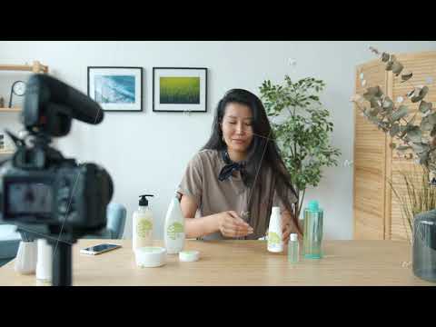 Attractive Asian girl vlogger speaking about organic cosmetics holding bottles using camera at home