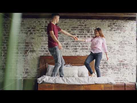 Young girlfriend and boyfriend are dancing on double bed and kissing having fun together in bedroom