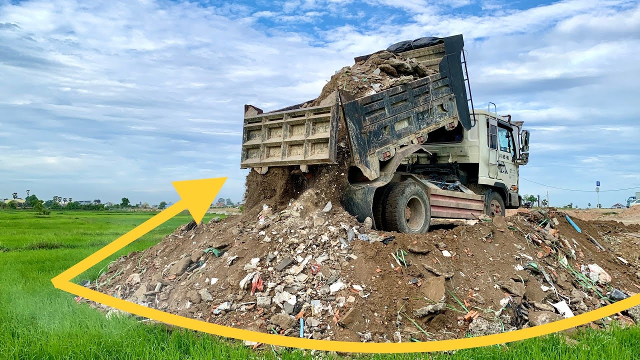 5 Ton dump trucks unload rocky soil to cover up a green Rice’s field ...