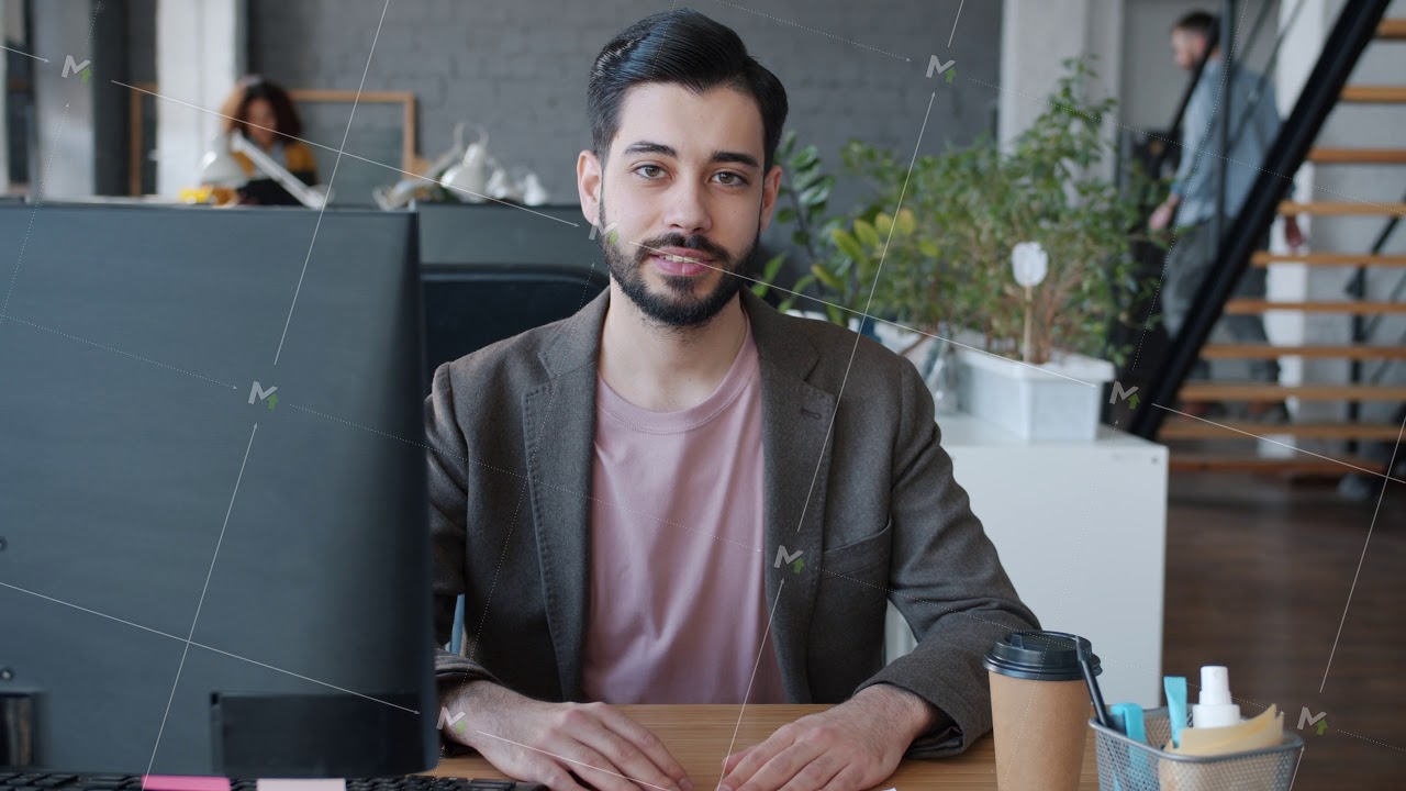 Portrait of Middle Eastern man smiling at computer desk in coworking ...