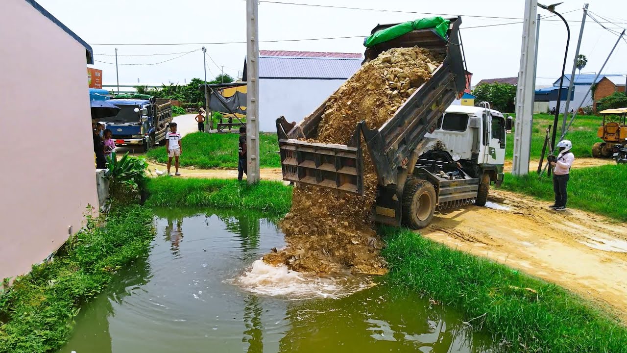 New Action Showing Trucks dumping soil into dirty water filled lake ...