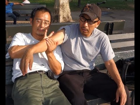 Luodong Massages Hispanic Man's Elbow On The Park Bench