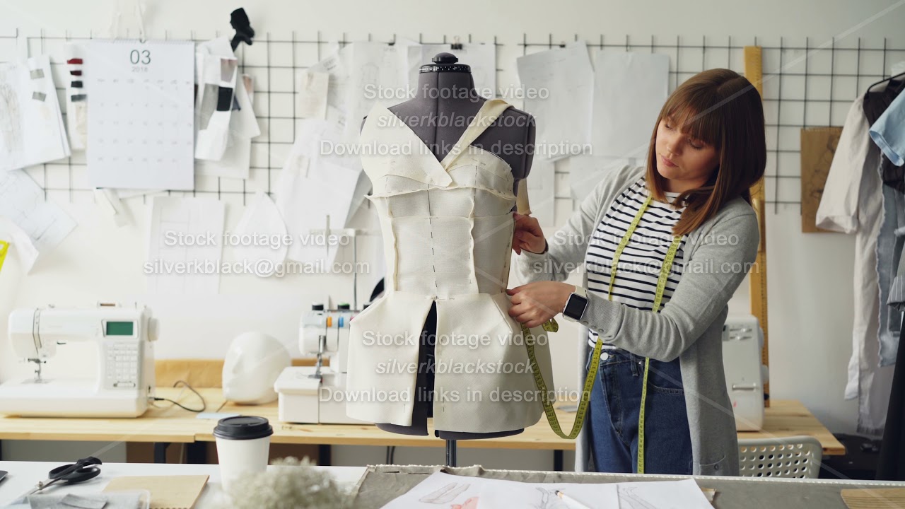 Young seamstress is measuring clothing pinned to tailoring dummy with ...
