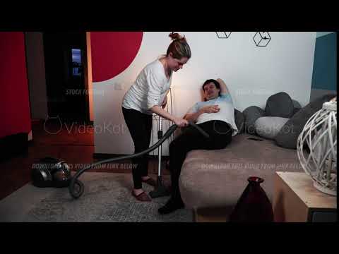 Pregnant woman is cleaning her man laying on sofa with vacuum cleaner