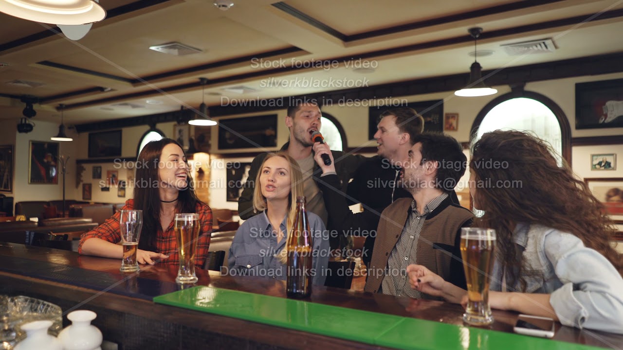 Happy young friends are singing karaoke while drinking beer in modern ...