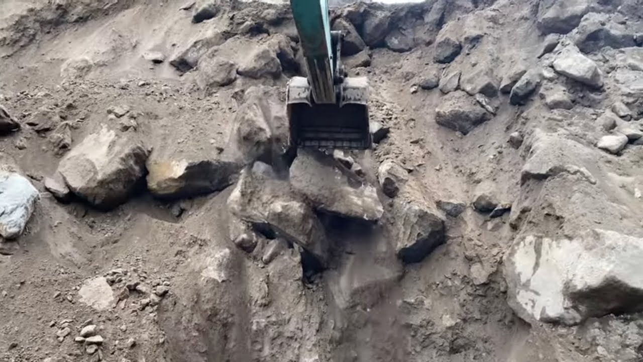 The excavator works to dig up rocks and sand to be loaded into the ...