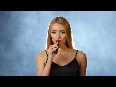 Blonde with red lips smokes an electronic cigarette and smiles  Black smoke background  Silhouette —