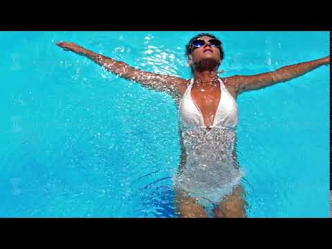 Aerial of beautiful toned young woman in white bikini and sunglasses swims in crystal clear water of