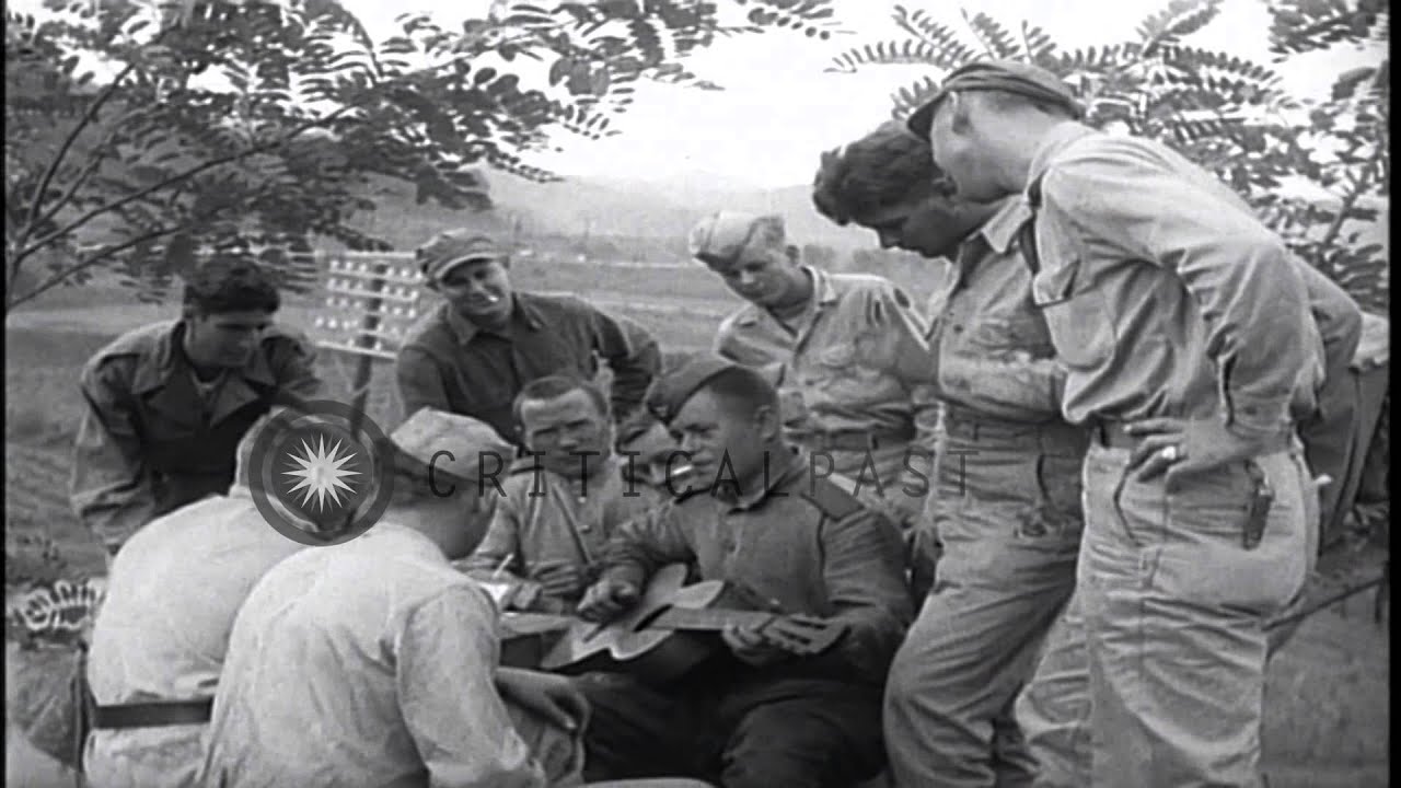 US and Russian soldiers gather round a fellow soldier who plays a ...