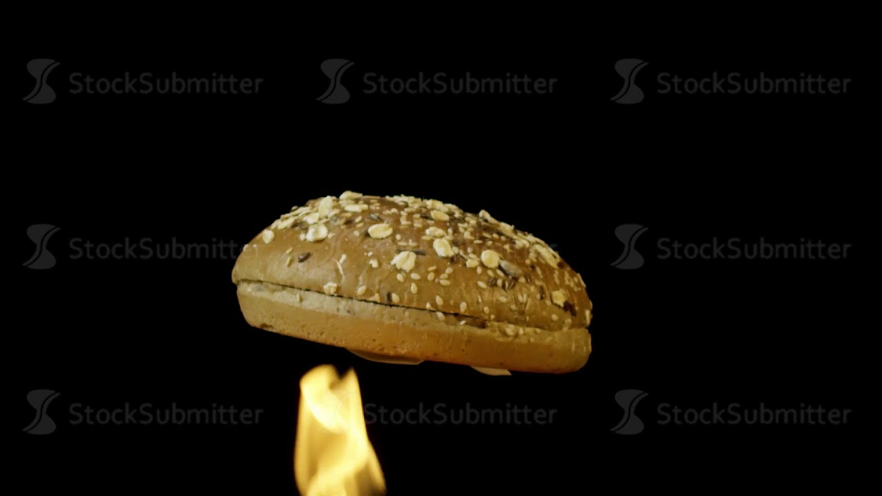 Close up of rotating burger bun in fire isolated on black background ...