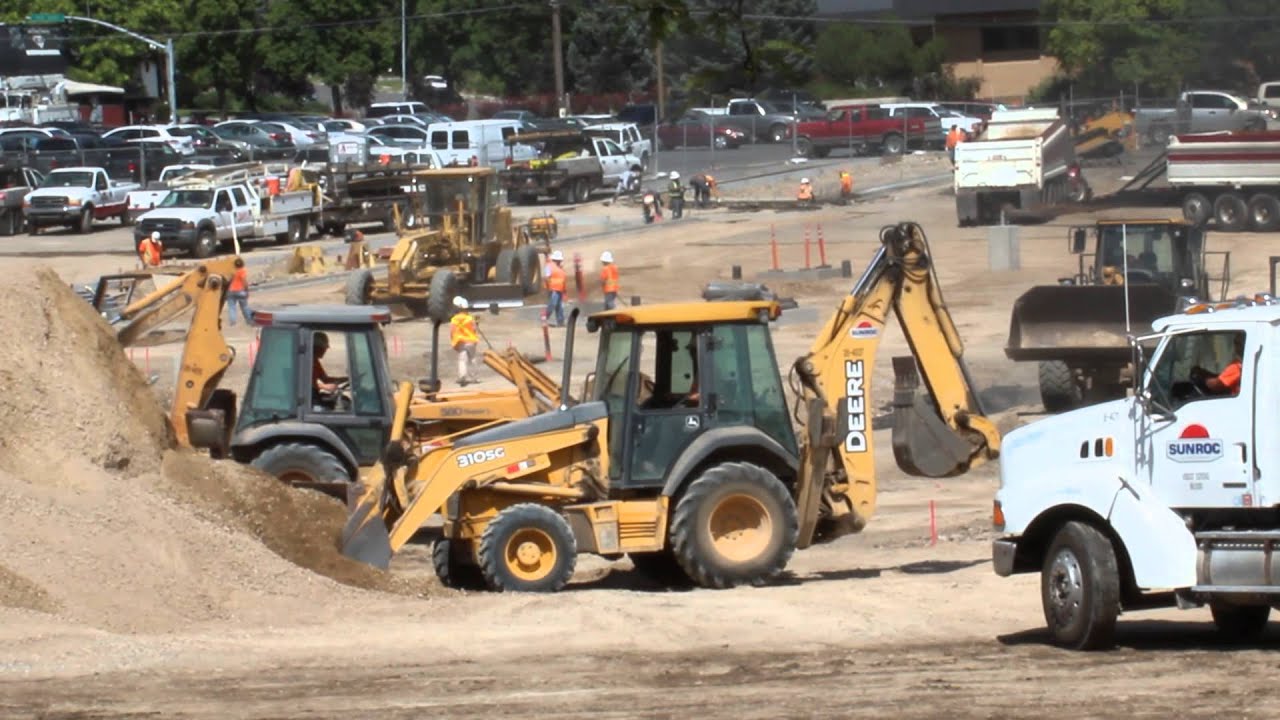 Backhoe digging with many work trucks working all around including a ...