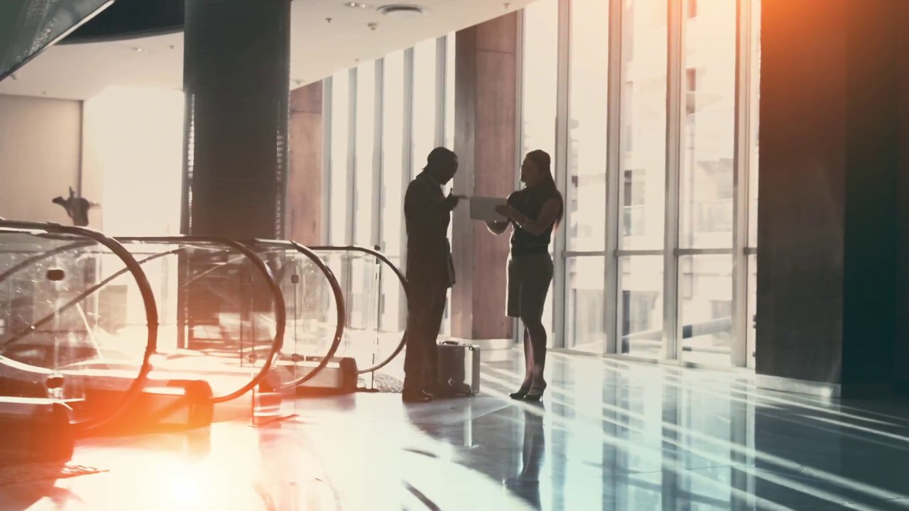 Handheld Shot Showing a Business Environment and Two People Standing in Front of Sunlit Windows ...
